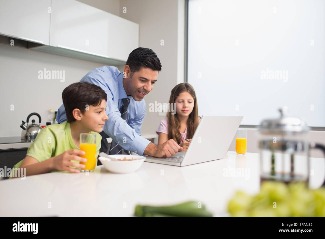 Father using laptop and kids having breakfast in kitchen Stock Photo ...