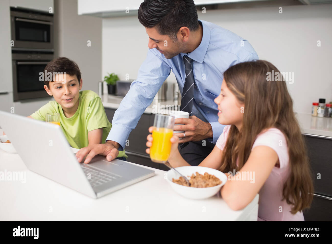 Father using laptop and kids having breakfast in kitchen Stock Photo ...