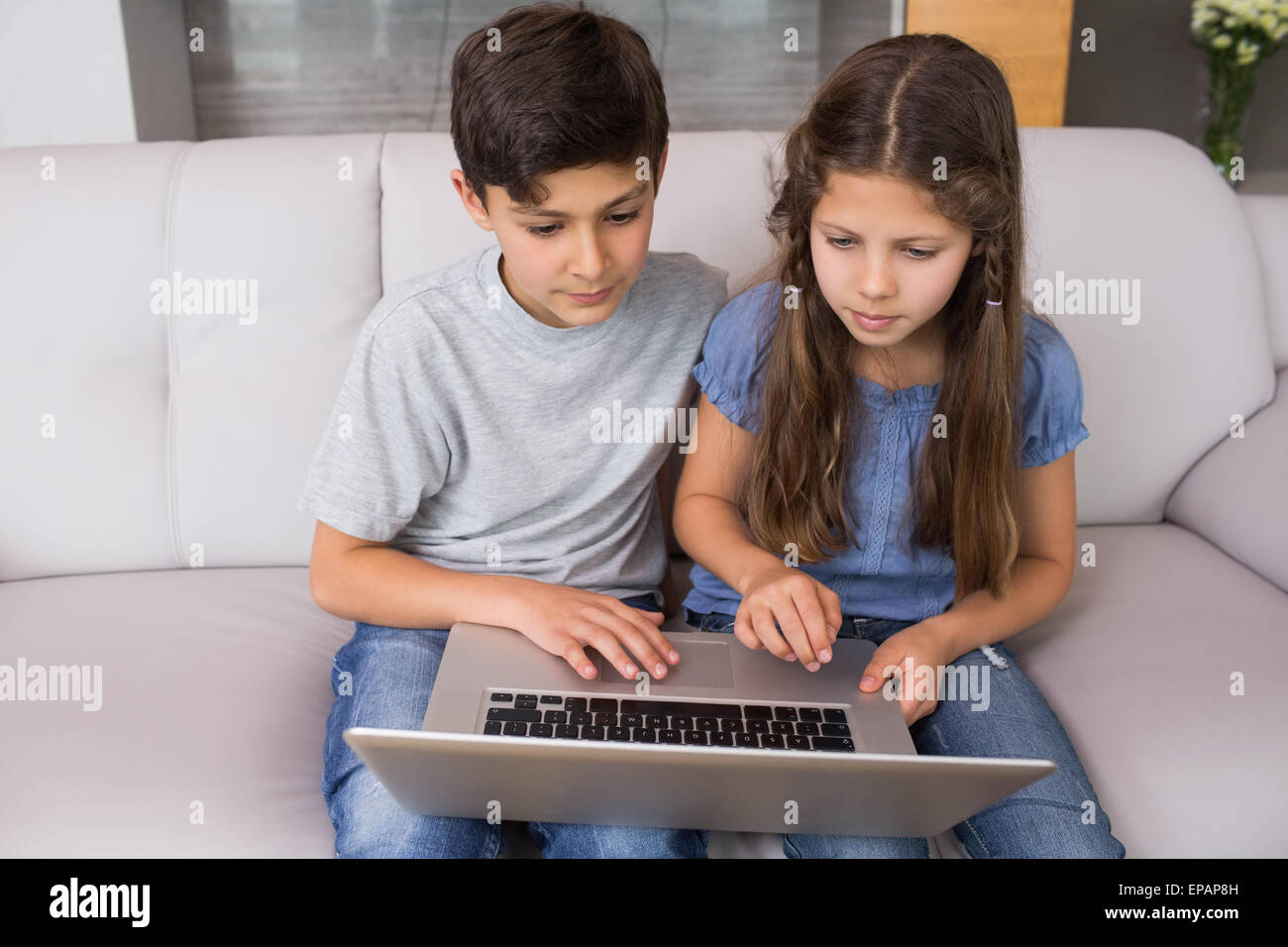 Young siblings using laptop in the living room Stock Photo - Alamy