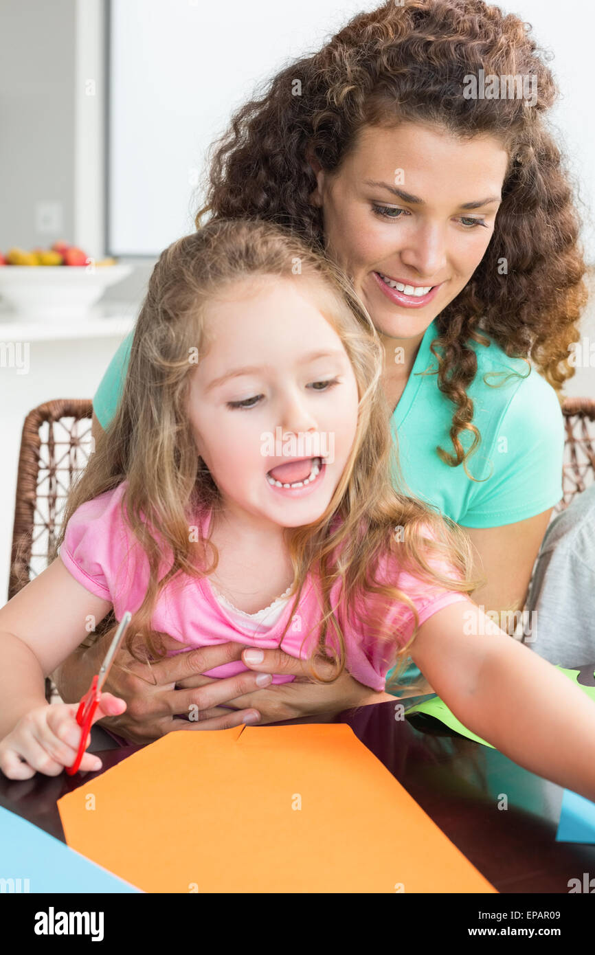 Cheerful little girl doing arts and crafts with mother at the table ...