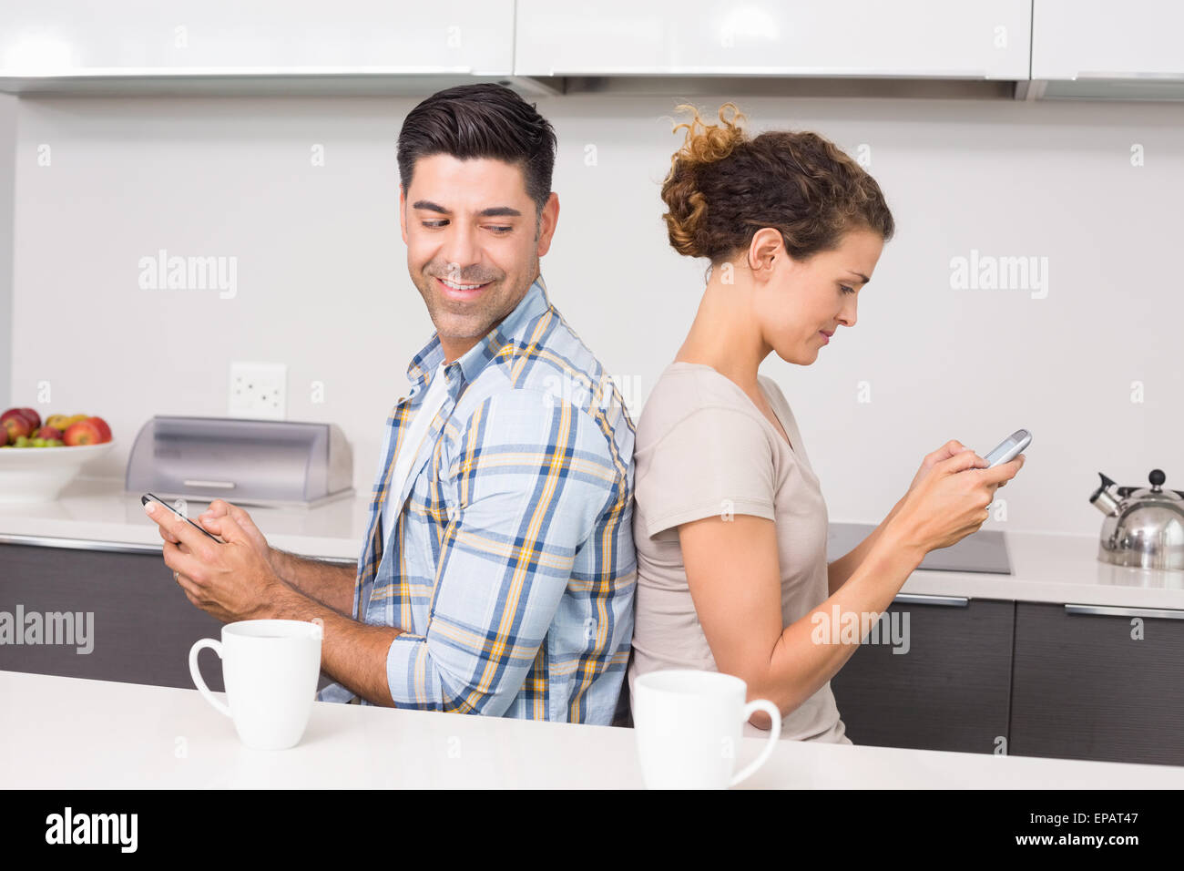 Happy couple sitting back to back texting Stock Photo - Alamy