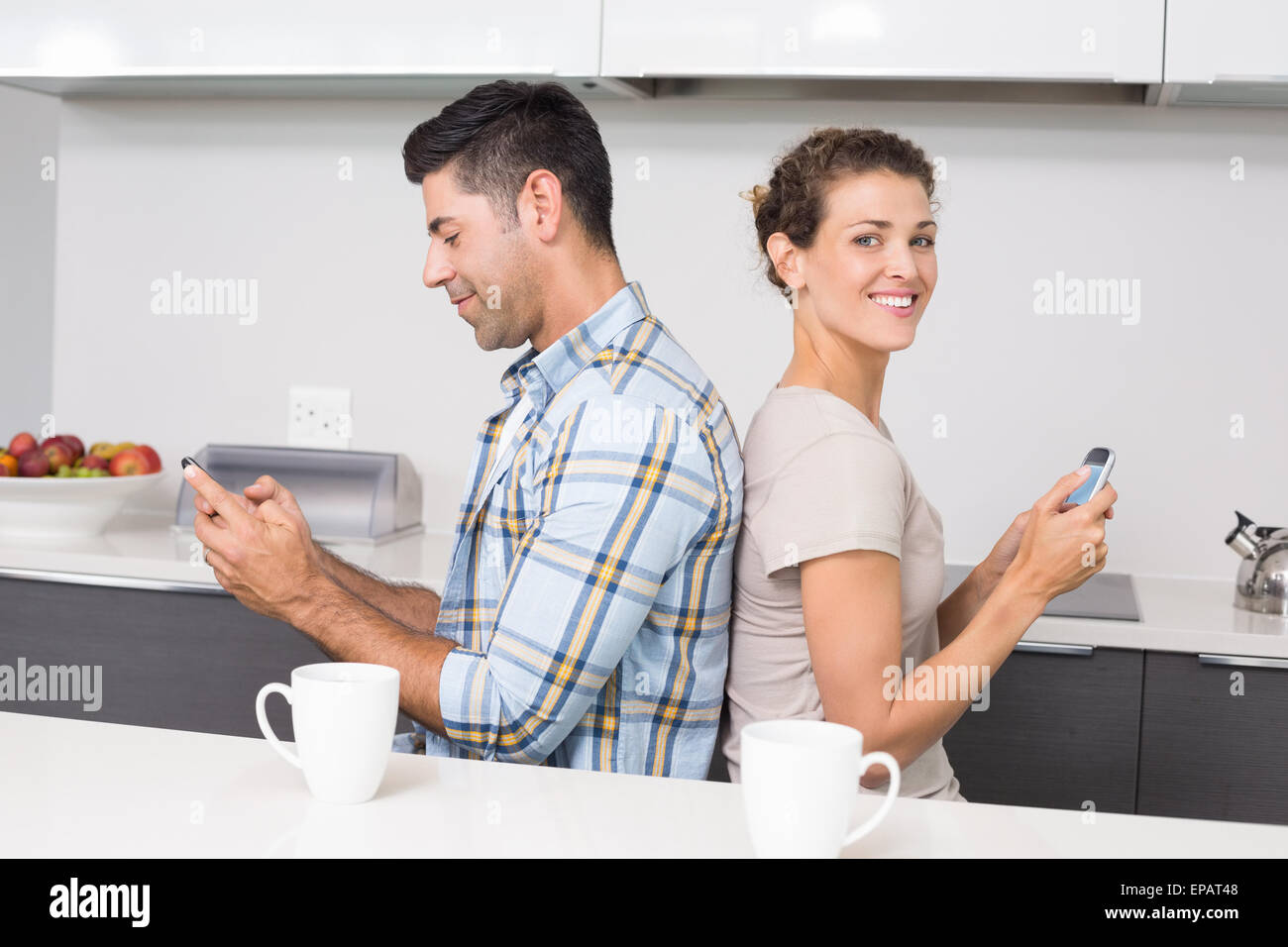 Smiling couple sitting back to back texting Stock Photo - Alamy