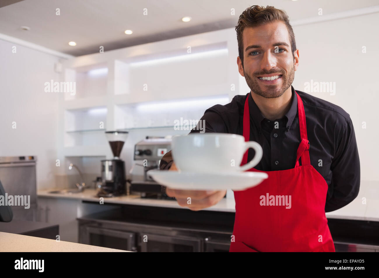 Happy barista offering cup of coffee to camera Stock Photo - Alamy