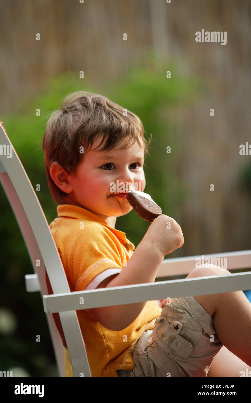 Boy sitting in chair eating popsicle Stock Photo - Alamy