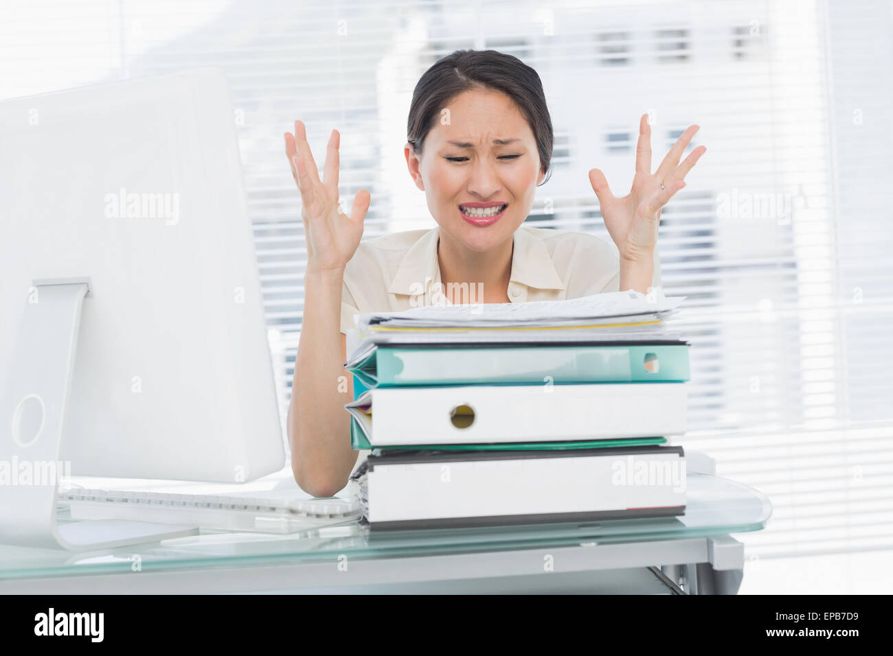 Angry young businesswoman sitting with stack of folders at office desk ...
