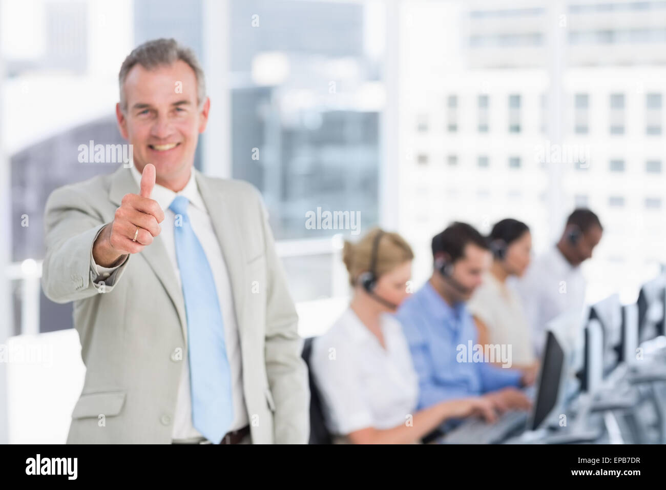 Businessman gesturing thumbs up with executives using computers Stock ...