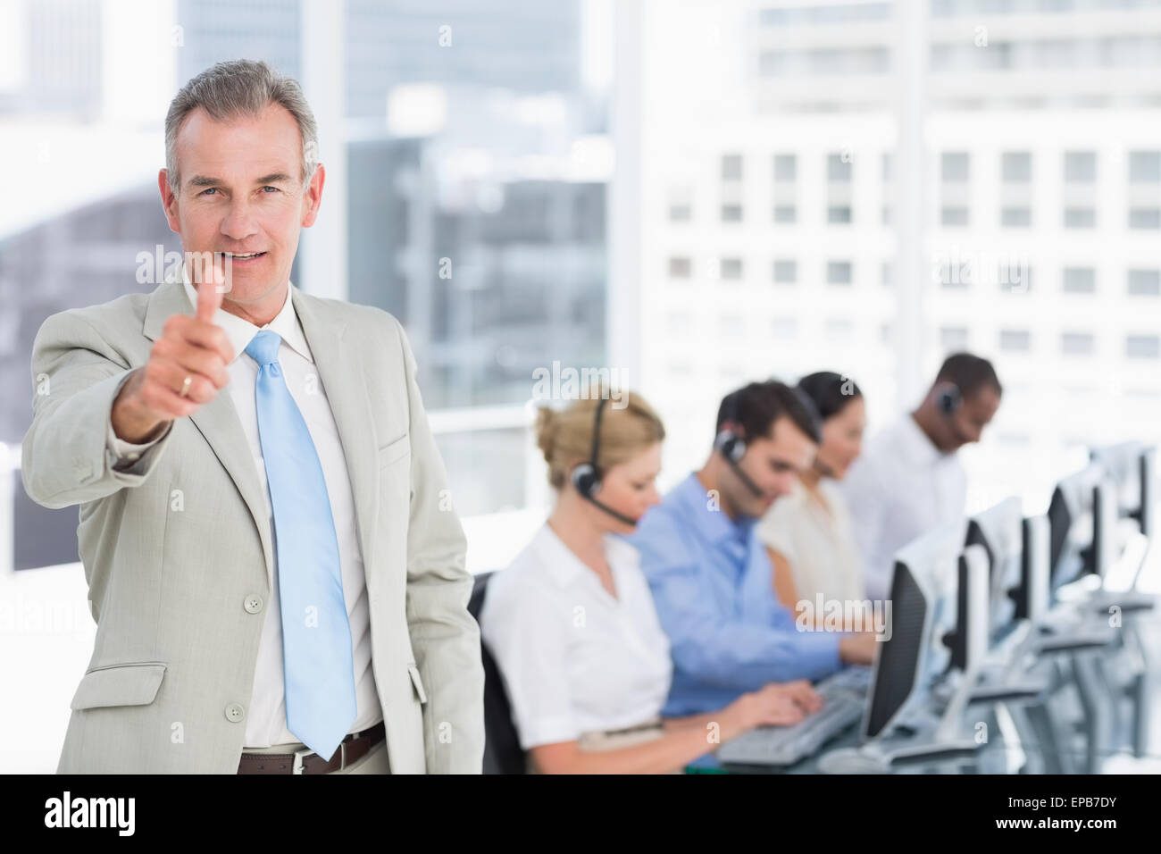 Businessman gesturing thumbs up with executives using computers Stock ...
