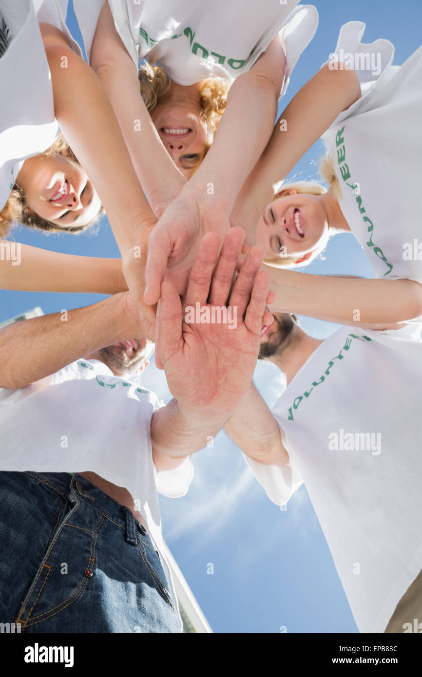 Happy volunteers with hands together against blue sky Stock Photo - Alamy