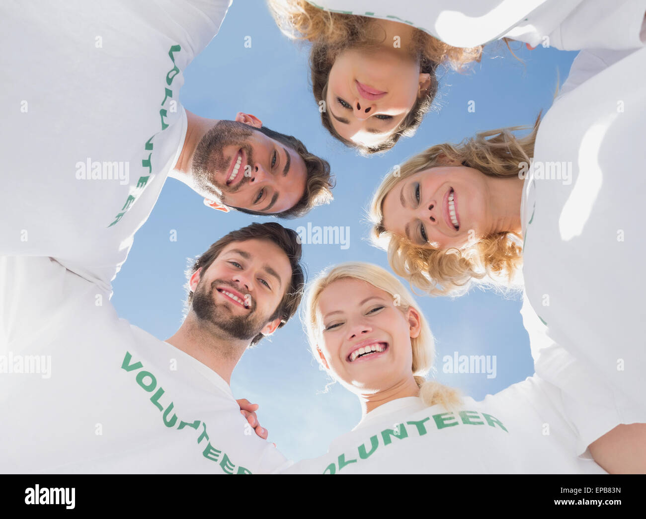 Happy volunteers forming a huddle against blue sky Stock Photo - Alamy