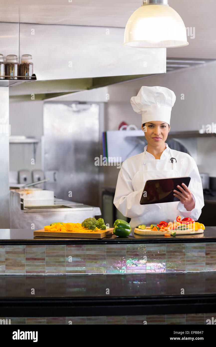Female chef using digital tablet while cutting vegetables in kitchen ...