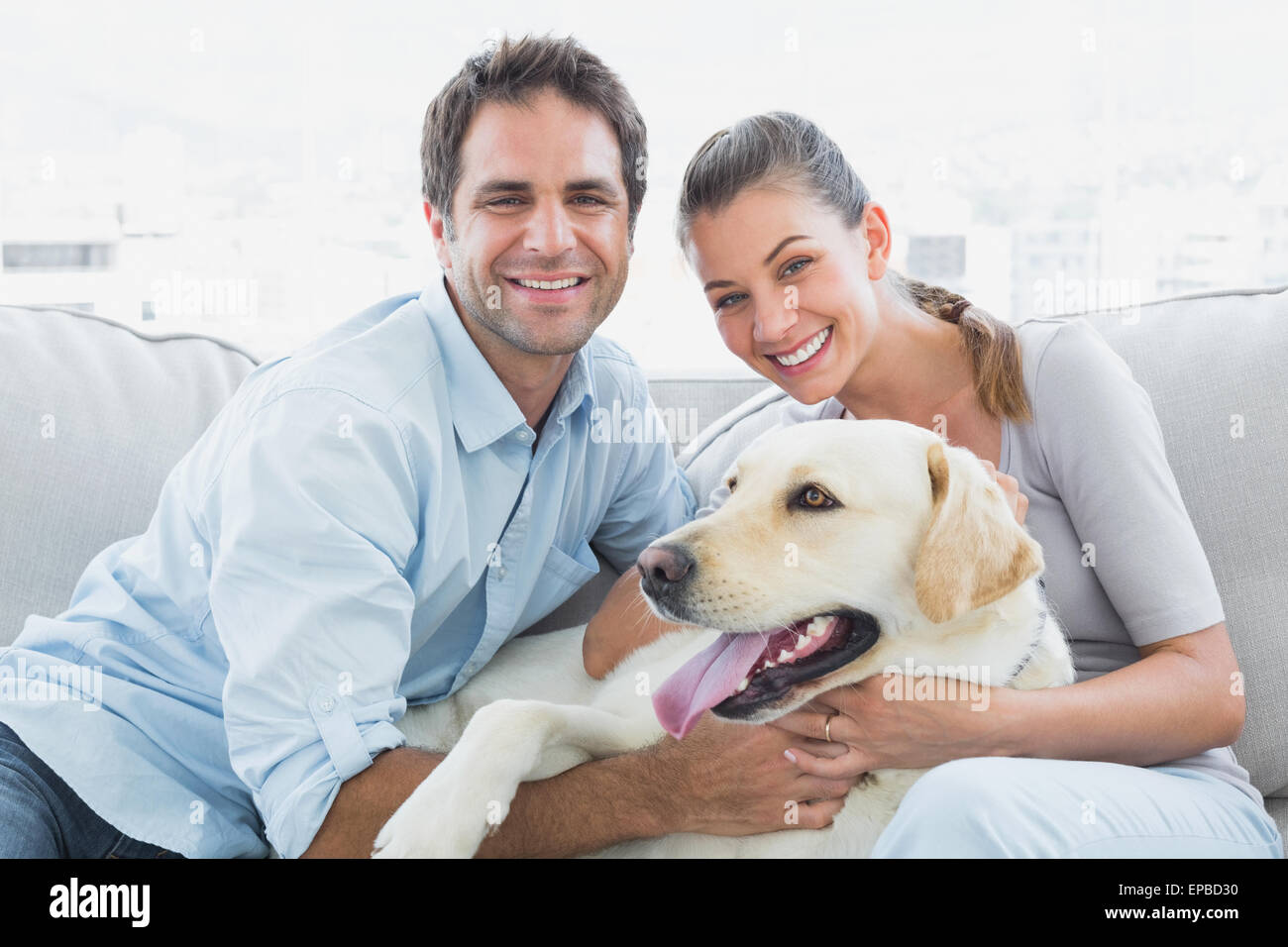 Smiling couple petting their yellow labrador on the couch Stock Photo ...