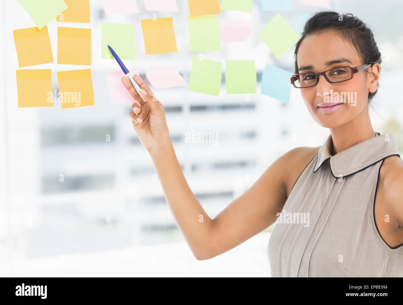 Designer pointing to sticky notes on window smiling at camera Stock ...