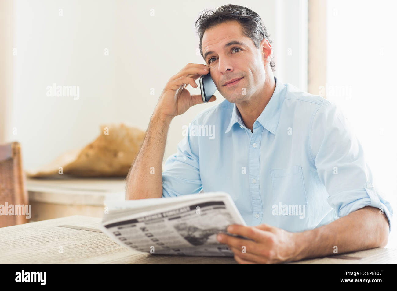 Man with newspaper using cellphone in kitchen Stock Photo - Alamy