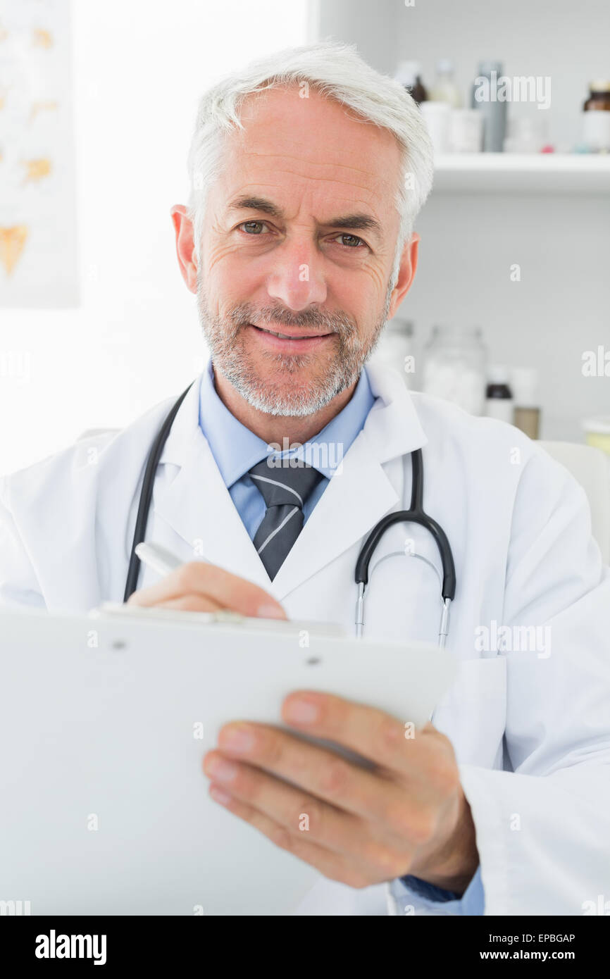 Smiling male doctor writing reports in medical office Stock Photo - Alamy