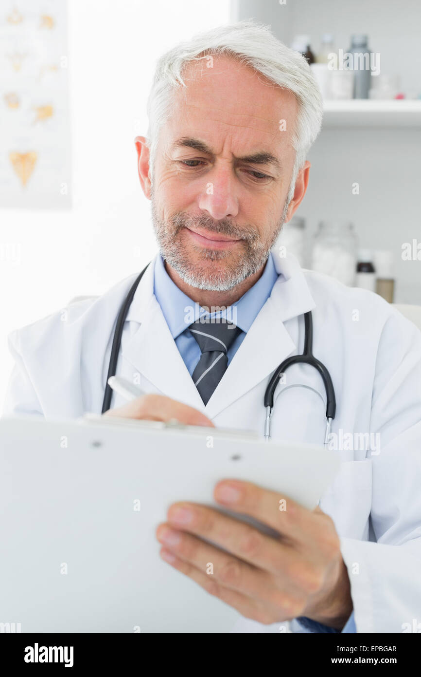Concentrated male doctor writing reports in clipboard at the hospital ...
