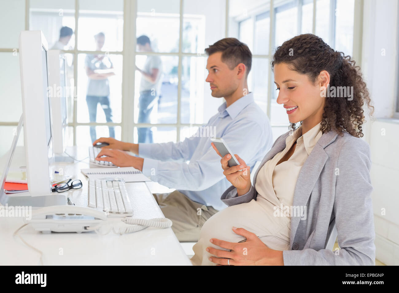 Casual pregnant businesswoman texting on phone at desk Stock Photo - Alamy