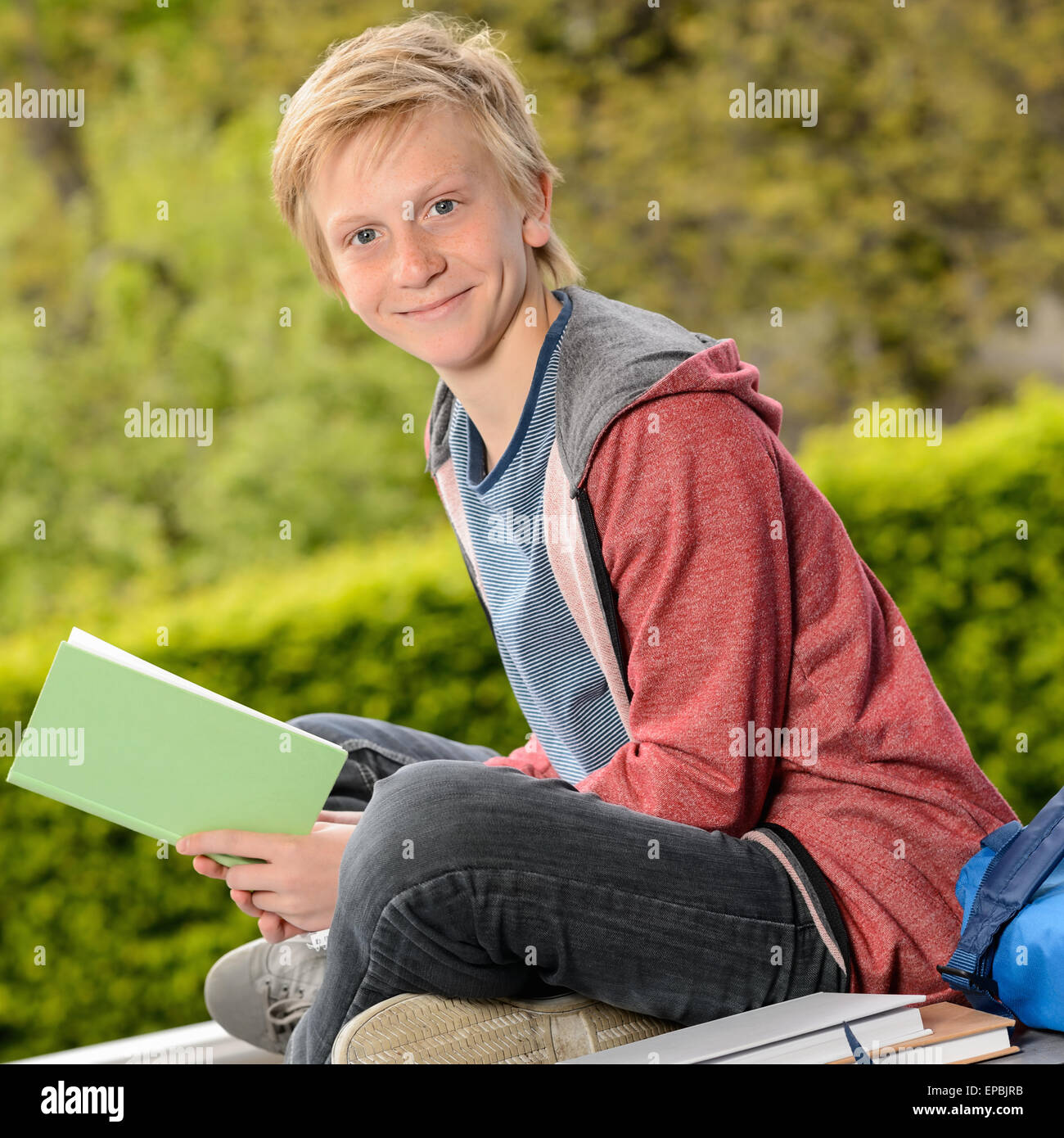 Student boy holding book sitting outside school Stock Photo - Alamy