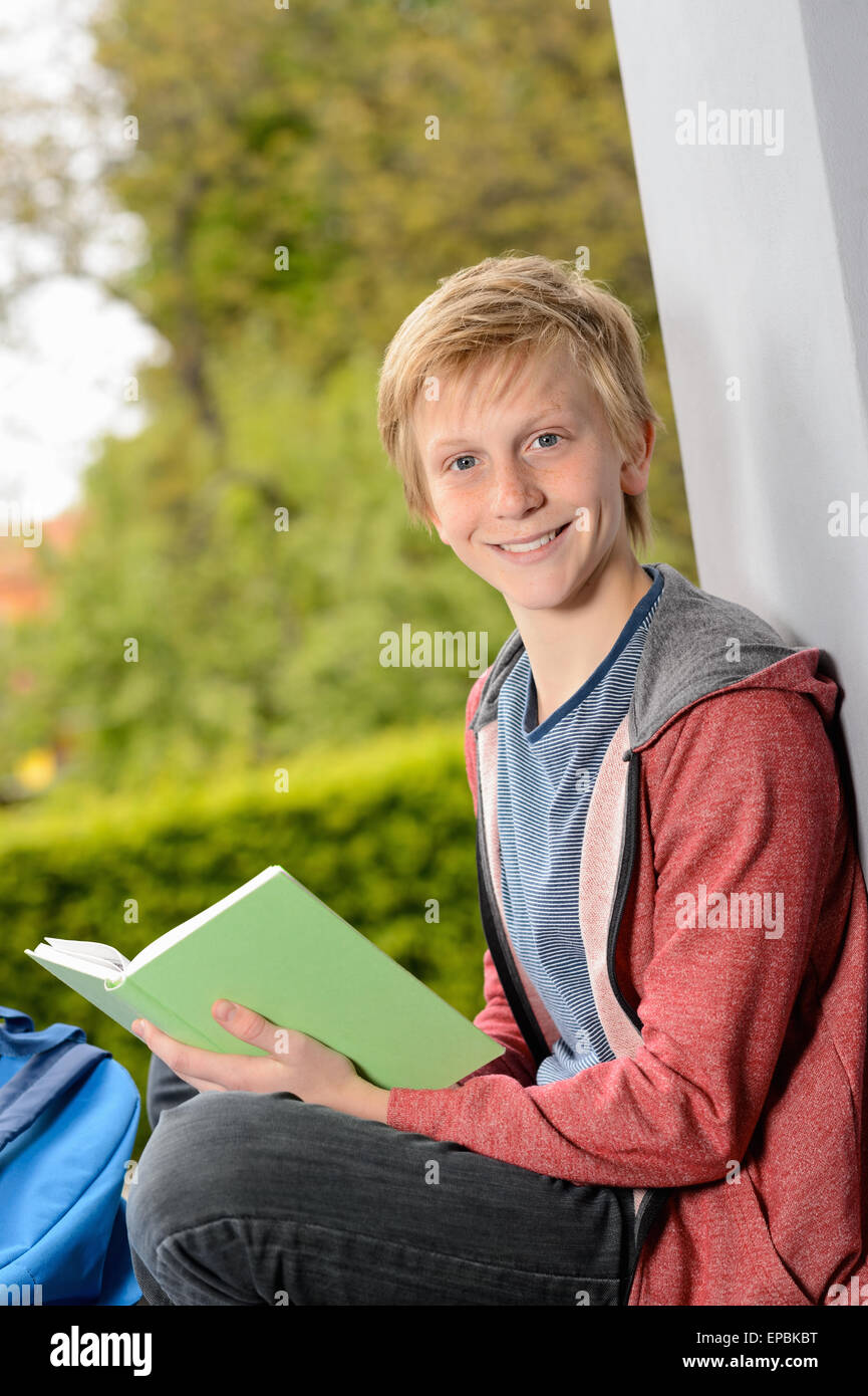 Happy boy sitting on wall with book Stock Photo - Alamy