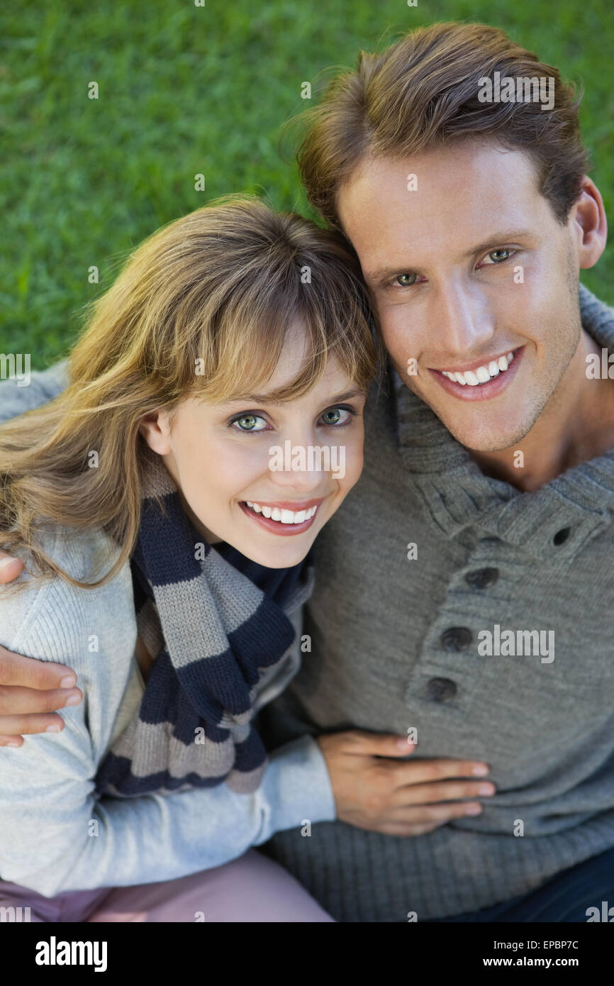 Cute couple sitting in the park embracing smiling at camera Stock Photo ...