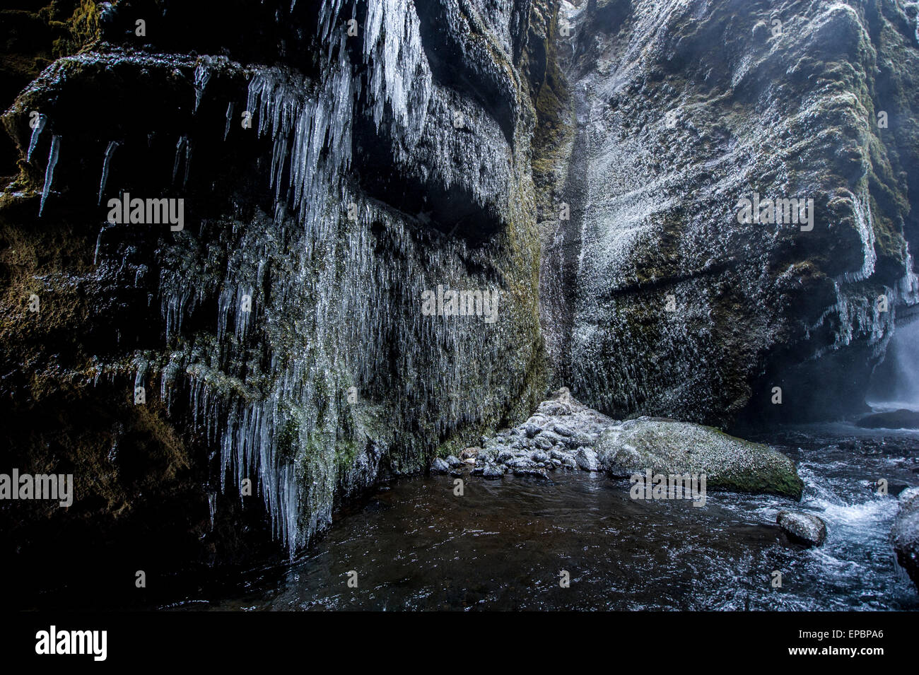 The interior of a cave with a waterfall and icicles covered by a frosty ...
