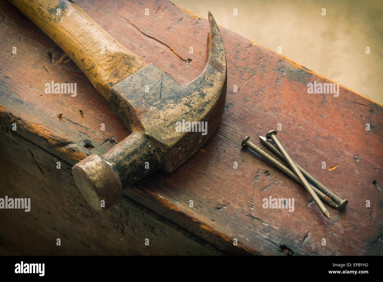 Old and worn contracting hammer and three nails on a distressed work ...