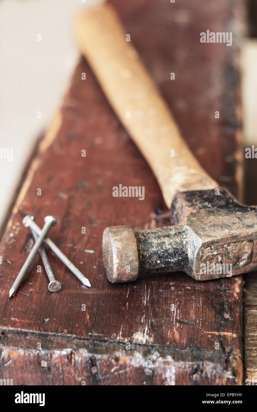 Old and worn contracting hammer and three nails on a distressed work ...