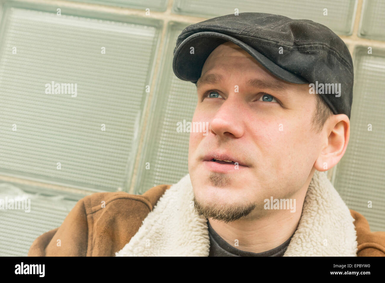 Cool guy in aviator jacket and newsie cap relaxes against a glass wall ...