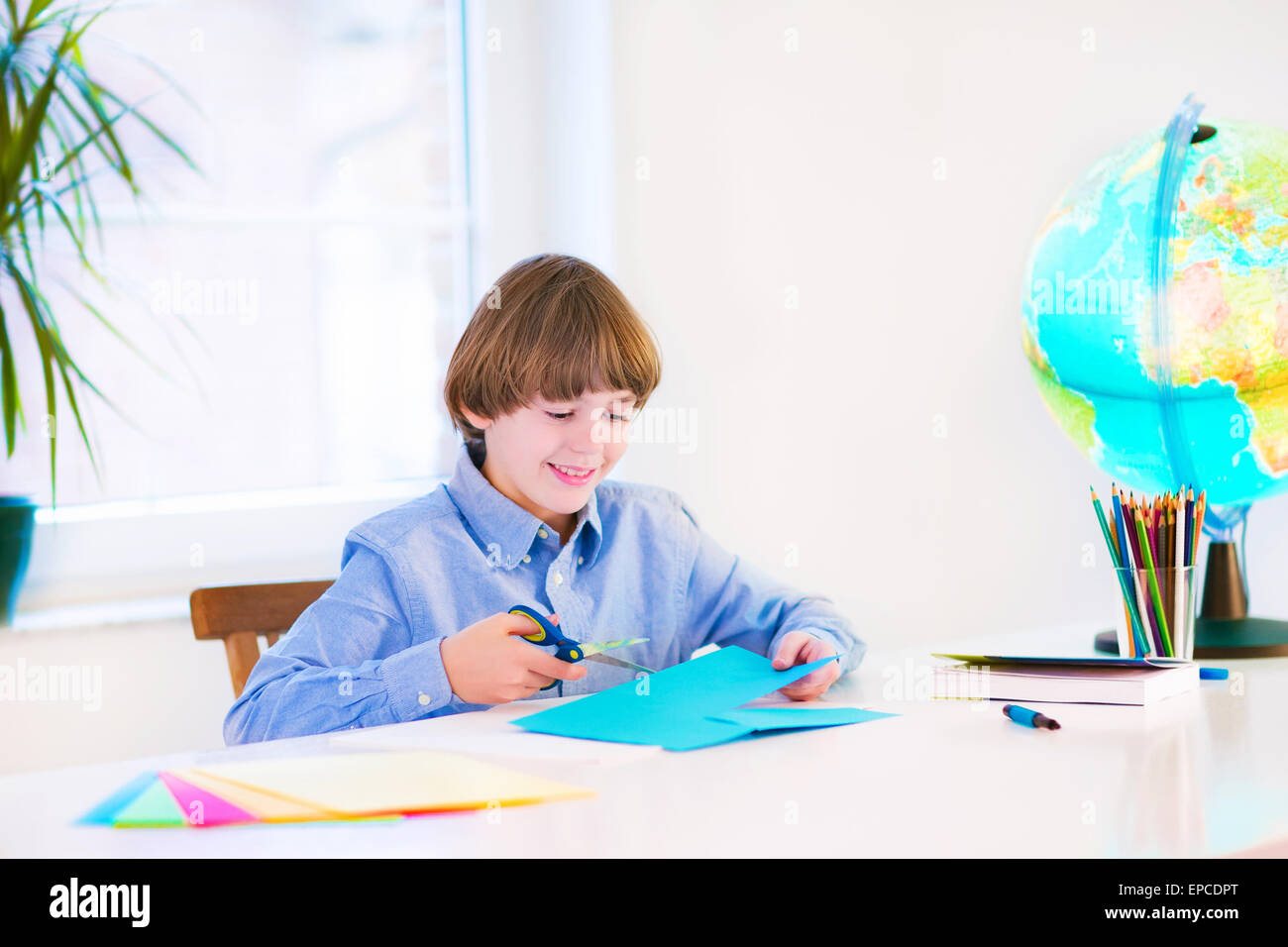 Happy smiling school boy, smart student, doing homework cutting paper ...