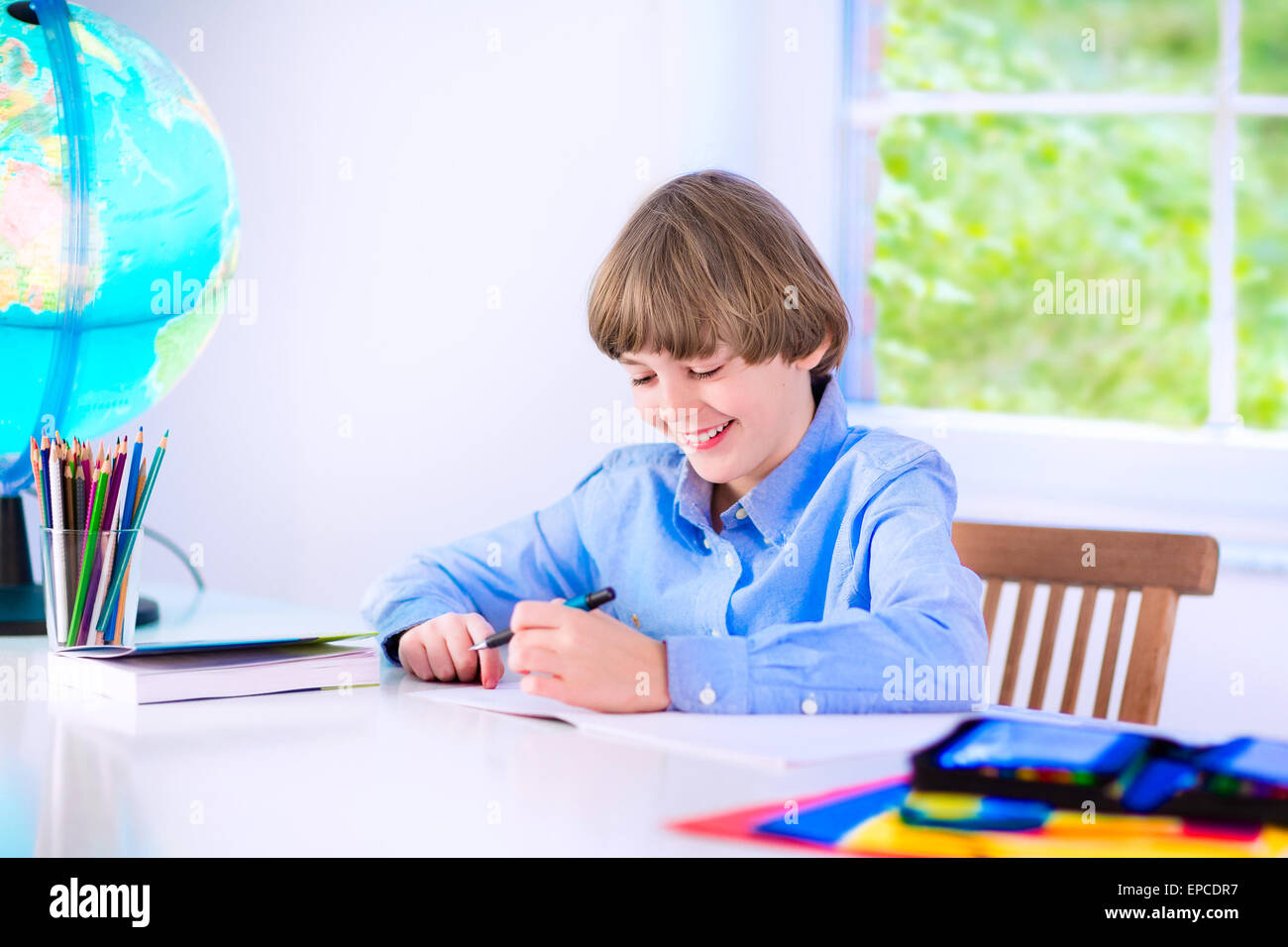 Happy smiling school boy, smart student, doing homework cutting paper ...