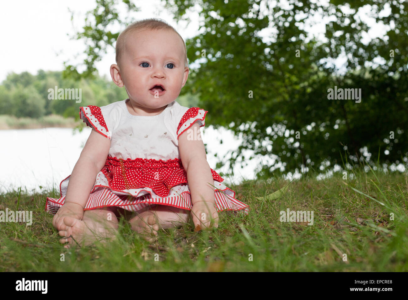 Little baby girl is sitting and playing near the lake Stock Photo - Alamy