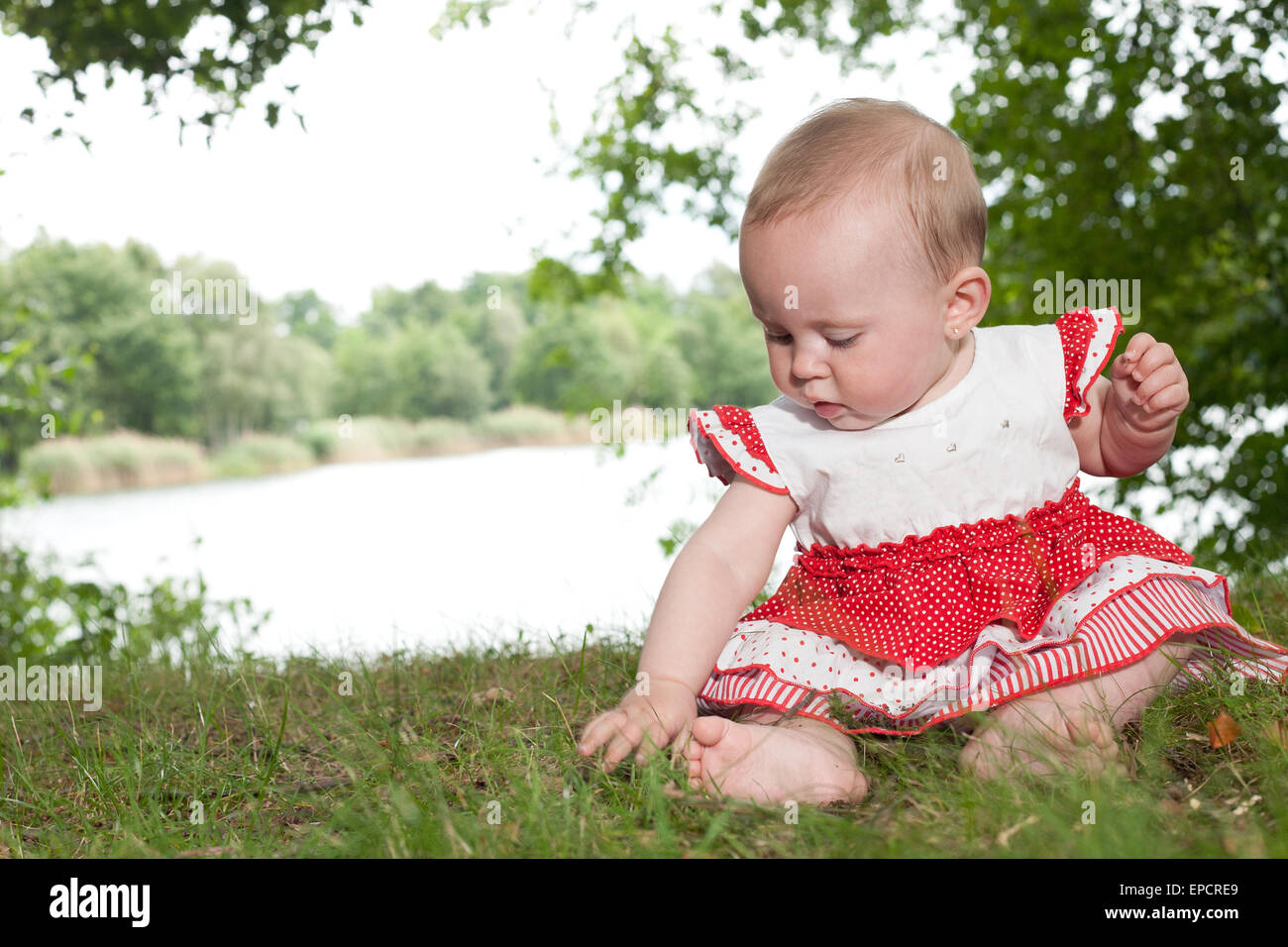 Little baby girl is sitting and playing near the lake Stock Photo - Alamy