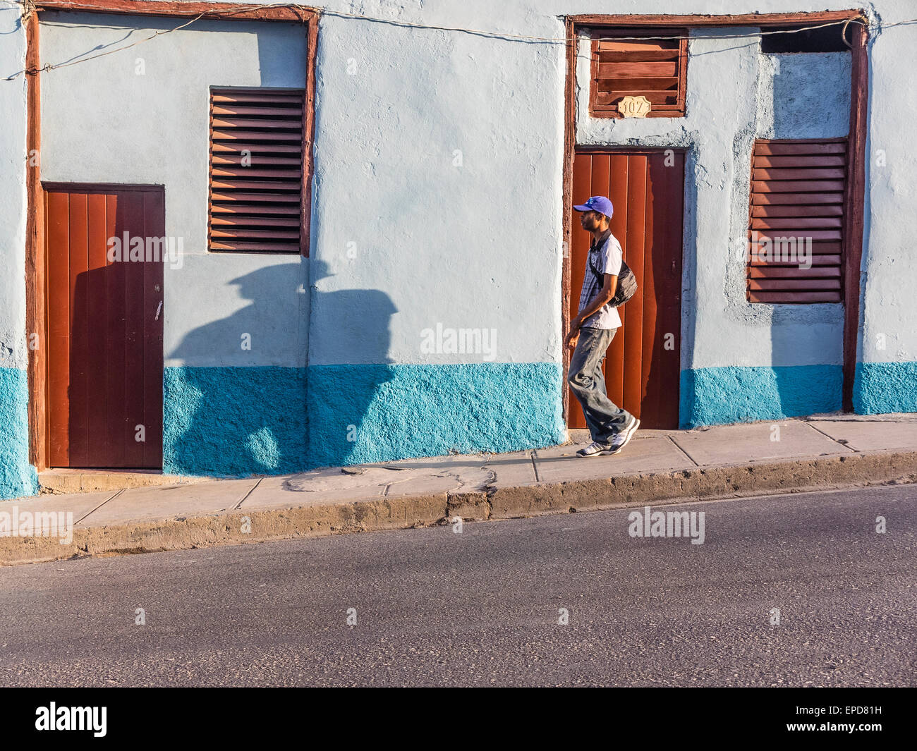 A young Cuban man casts a large shadow on a colorful wall at sunrise in ...