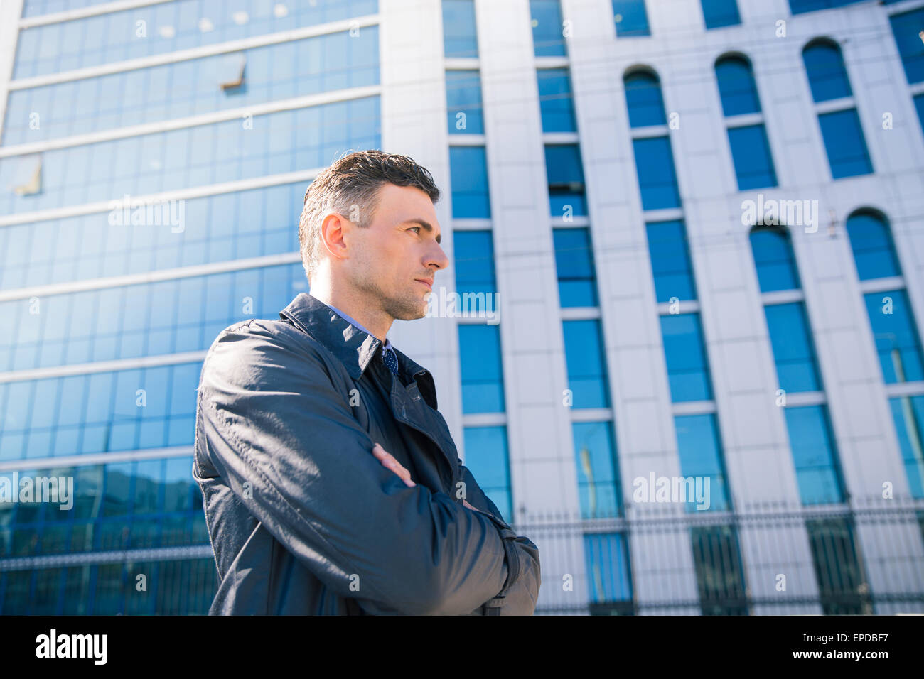 Side view portrait of a businessman standing with arms folded outdoors ...