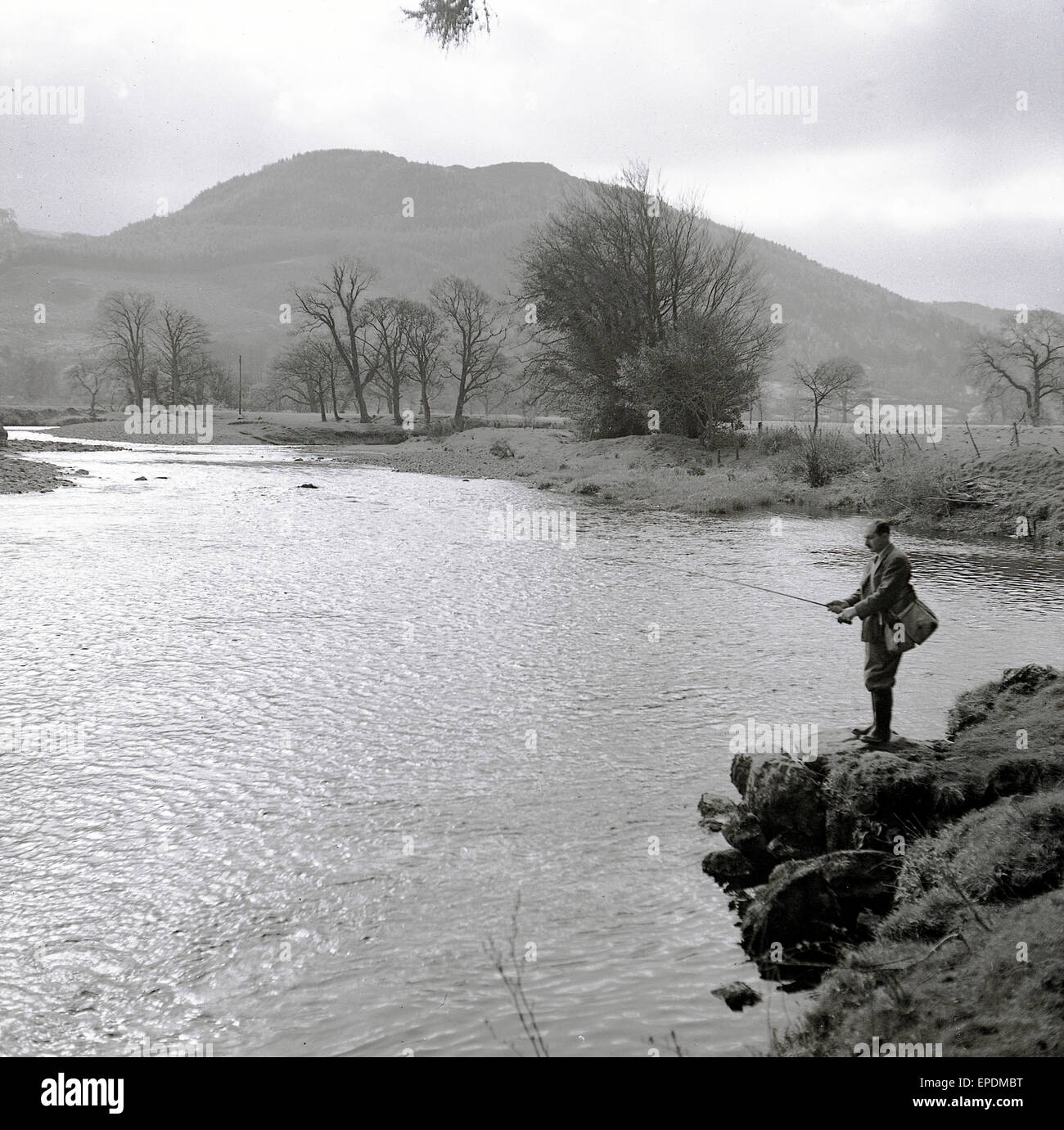 1950s, historical. a gentleman fishing in a lake, with satchel around ...