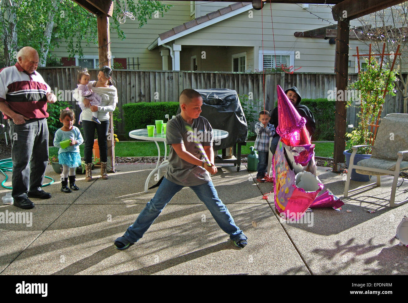 family watches son hit pinata on backyard patio Stock Photo - Alamy