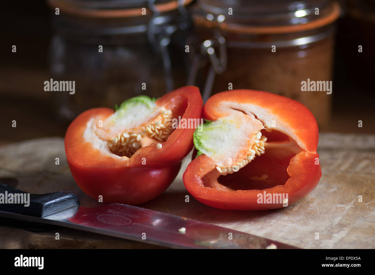 A red pepper, cut in half, on a chopping board, ready to cook with ...