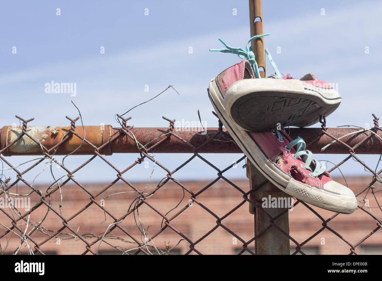 Pair of old worn classic sneakers hang from rusty chain link fence ...