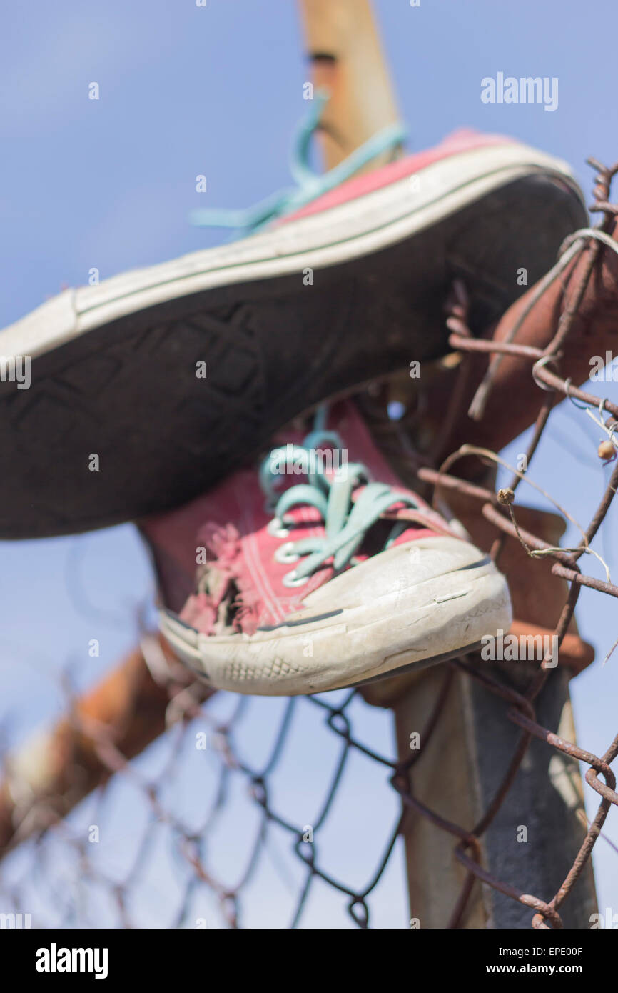 Pair of old worn classic sneakers hang from rusty chain link fence ...