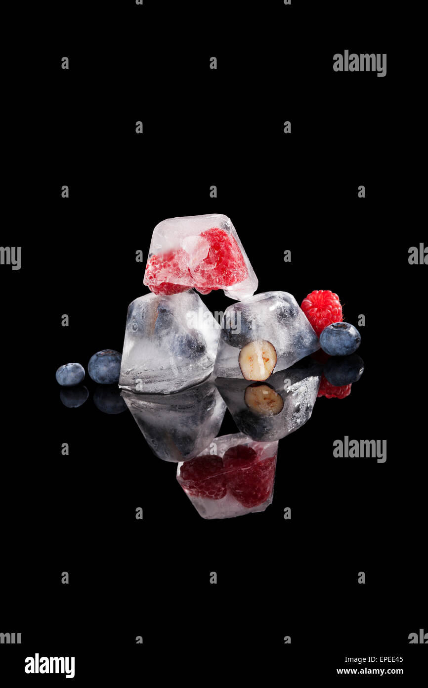Blueberries and raspberries frozen in ice cubes black background. Fresh ...
