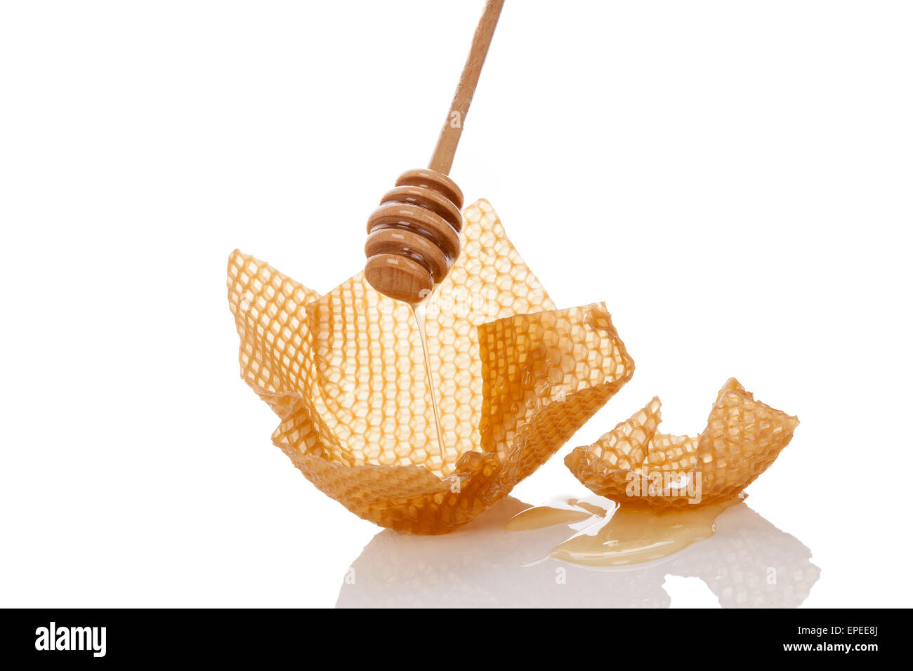 Honey dropping from wooden honey dipper onto honey comb isolated on ...