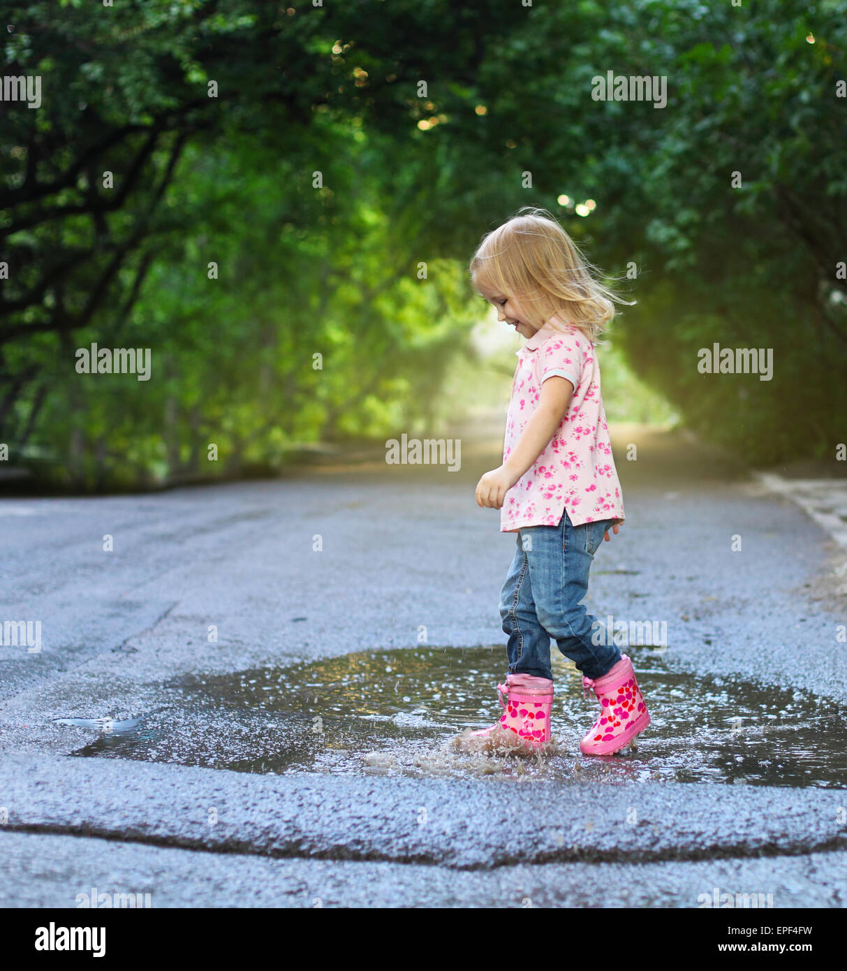 Cute little girl jumping into a puddle Stock Photo - Alamy