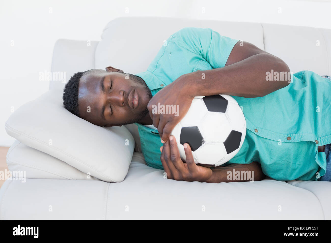 Football fan hugging ball on couch Stock Photo - Alamy
