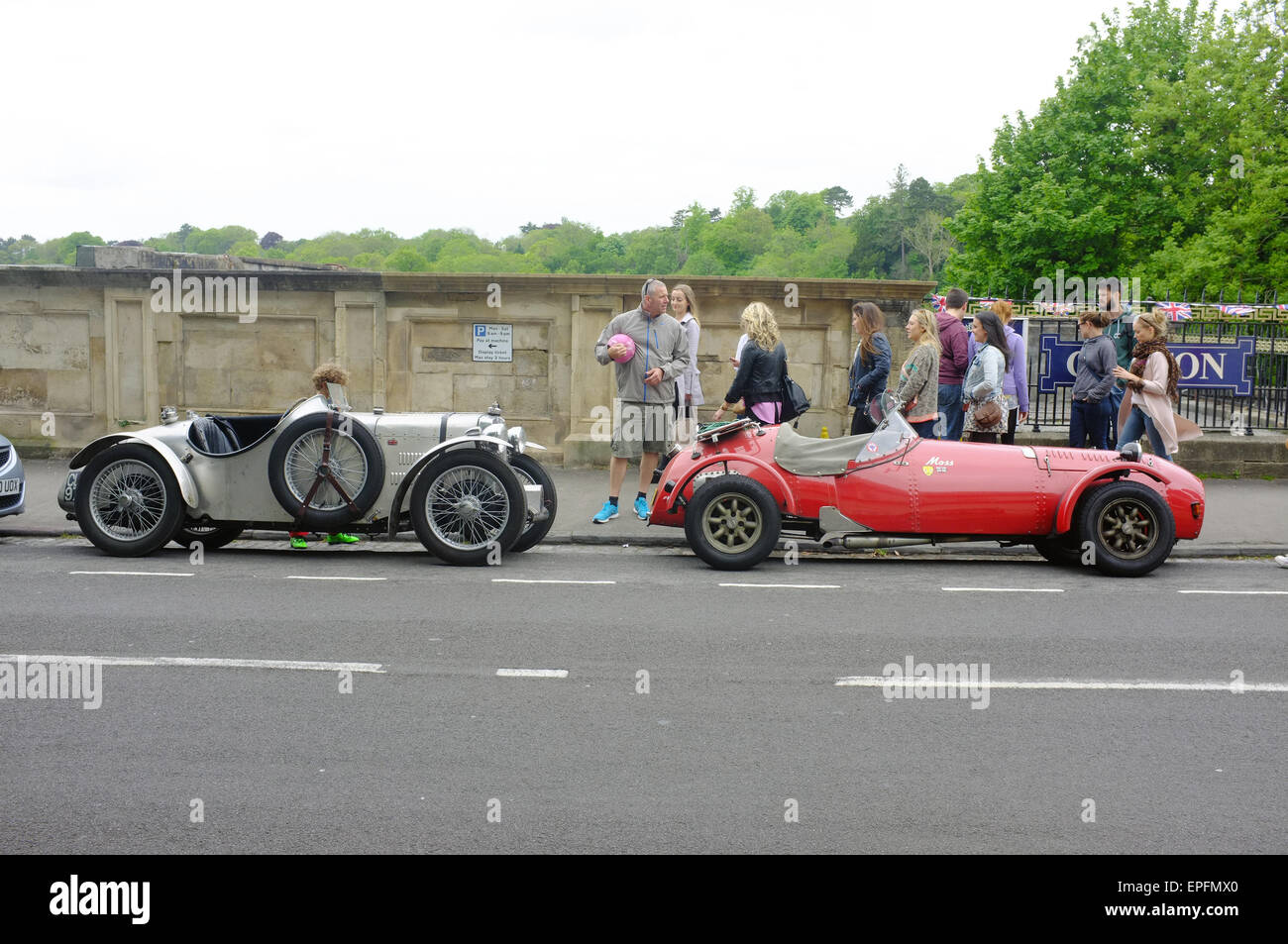 A group of car enthusiasts gather around two classic cars near the ...