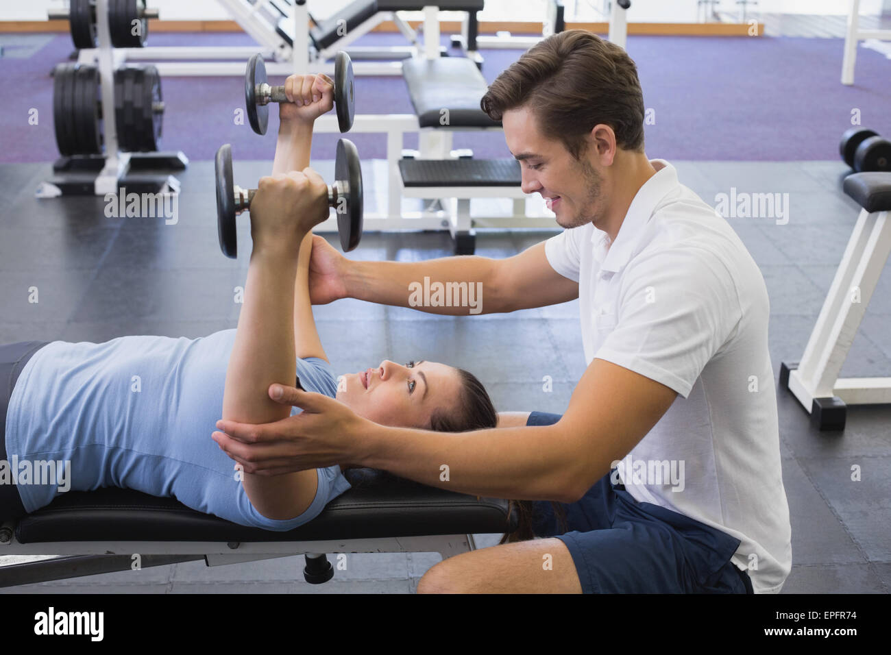 Personal trainer helping client lift dumbbells Stock Photo - Alamy