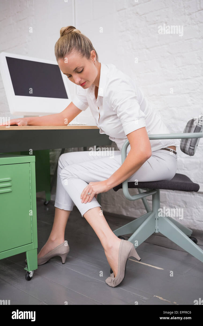 Businesswoman suffering from leg pain at office desk Stock Photo - Alamy