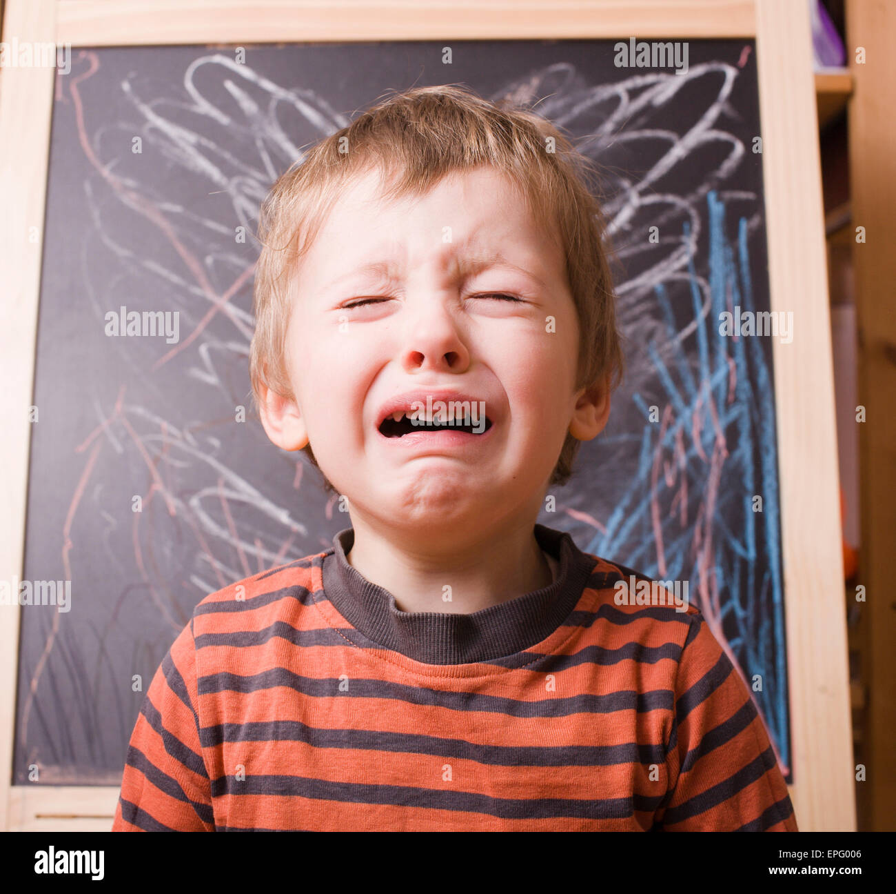 little cute boy screaming and crying at school near blackboard close up ...