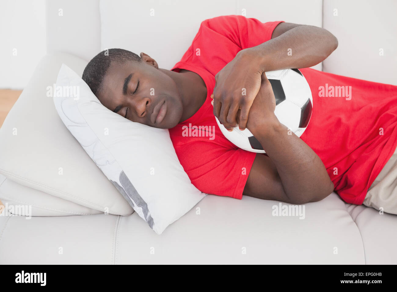 Football fan sleeping on couch hugging ball Stock Photo - Alamy