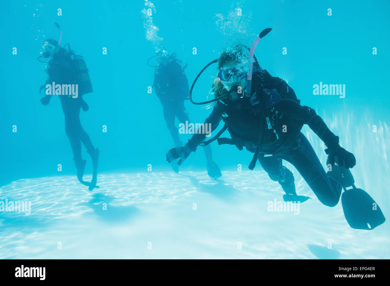 Friends on scuba training submerged in swimming pool one looking to ...