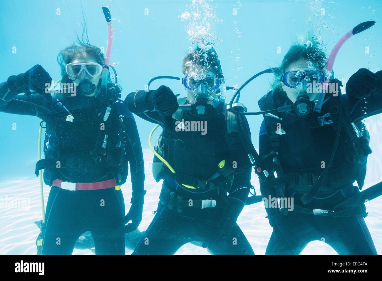 Friends on scuba training submerged in swimming pool showing thumbs ...
