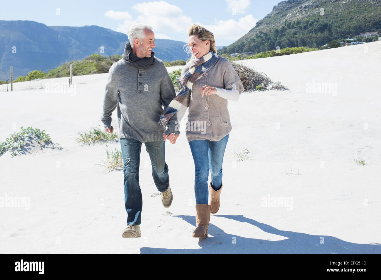 Smiling couple skipping on the beach in warm clothing Stock Photo - Alamy
